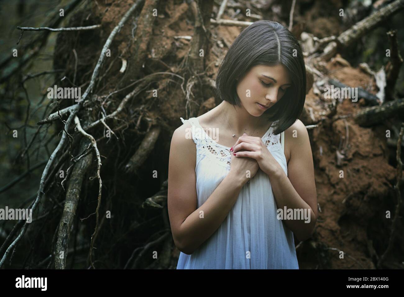Sad and beautiful woman praying among dead tree roots . Dark fantasy ...