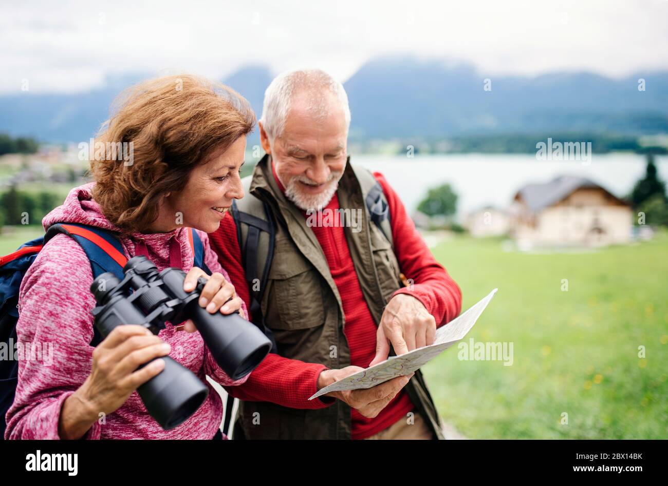 Senior pensioner couple with hiking in nature, using binoculars and map ...