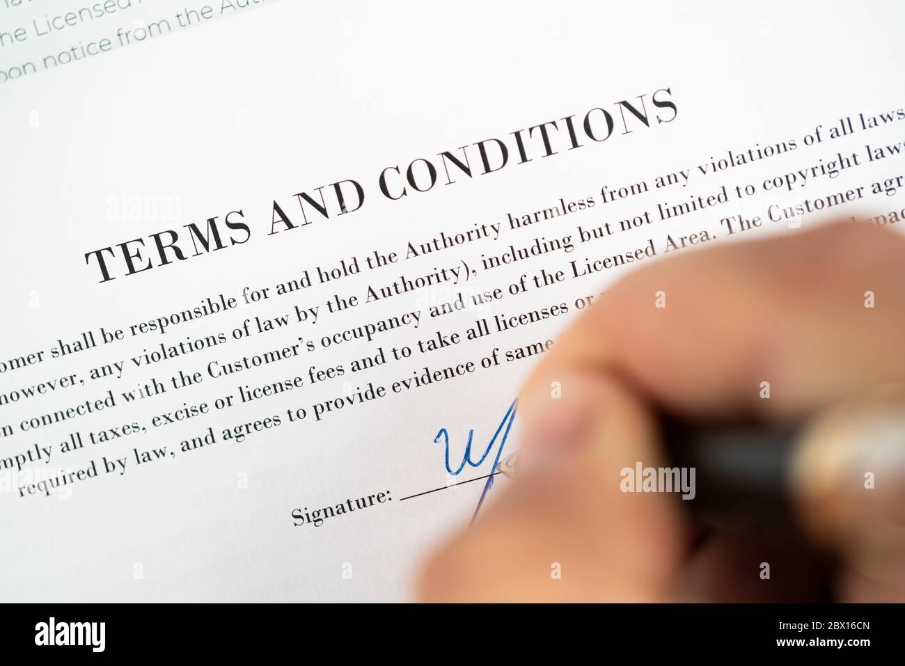 Close up hand with pen on the signature line on a terms and conditions ...
