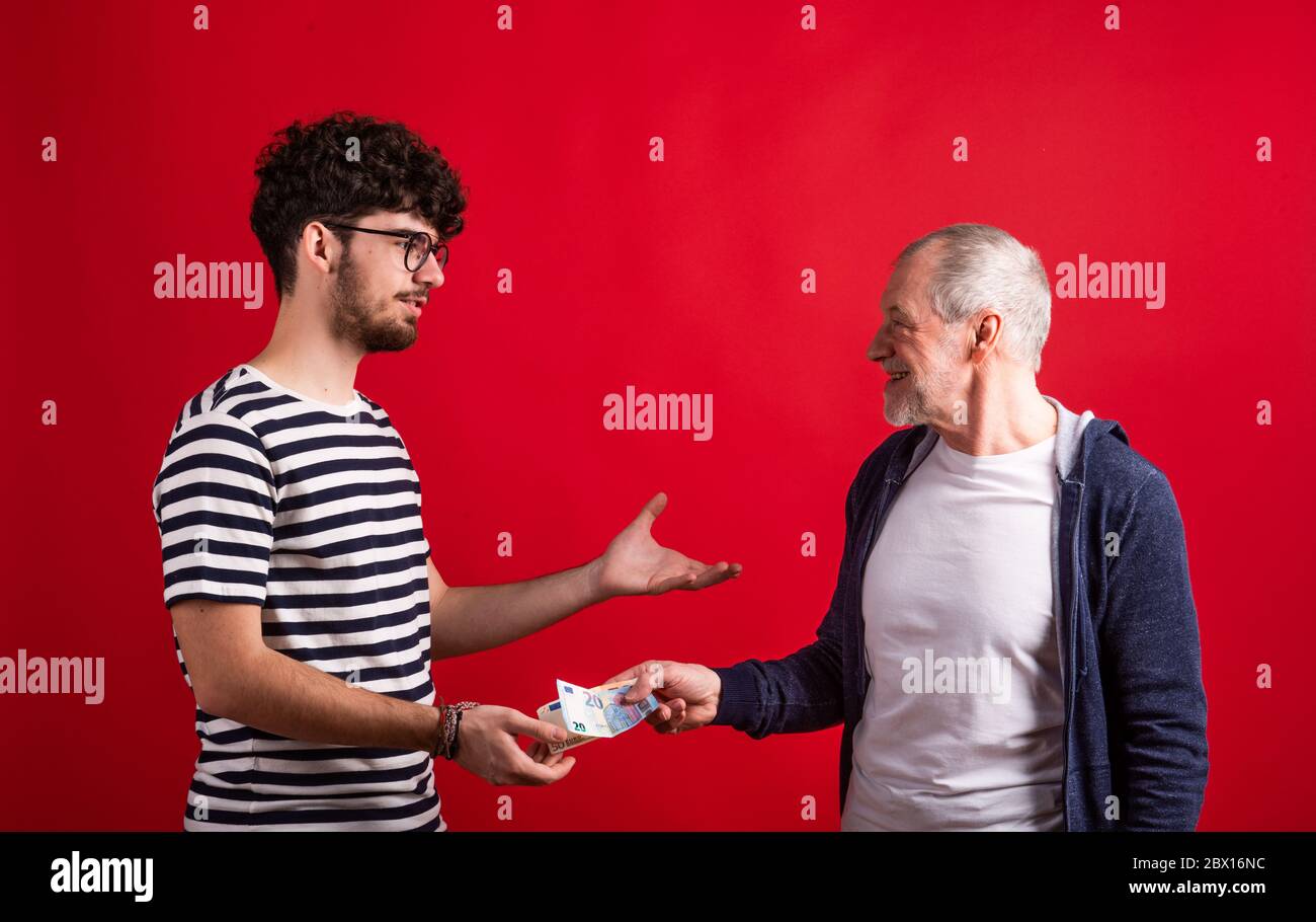 Senior father giving money to his son in a studio on red background ...
