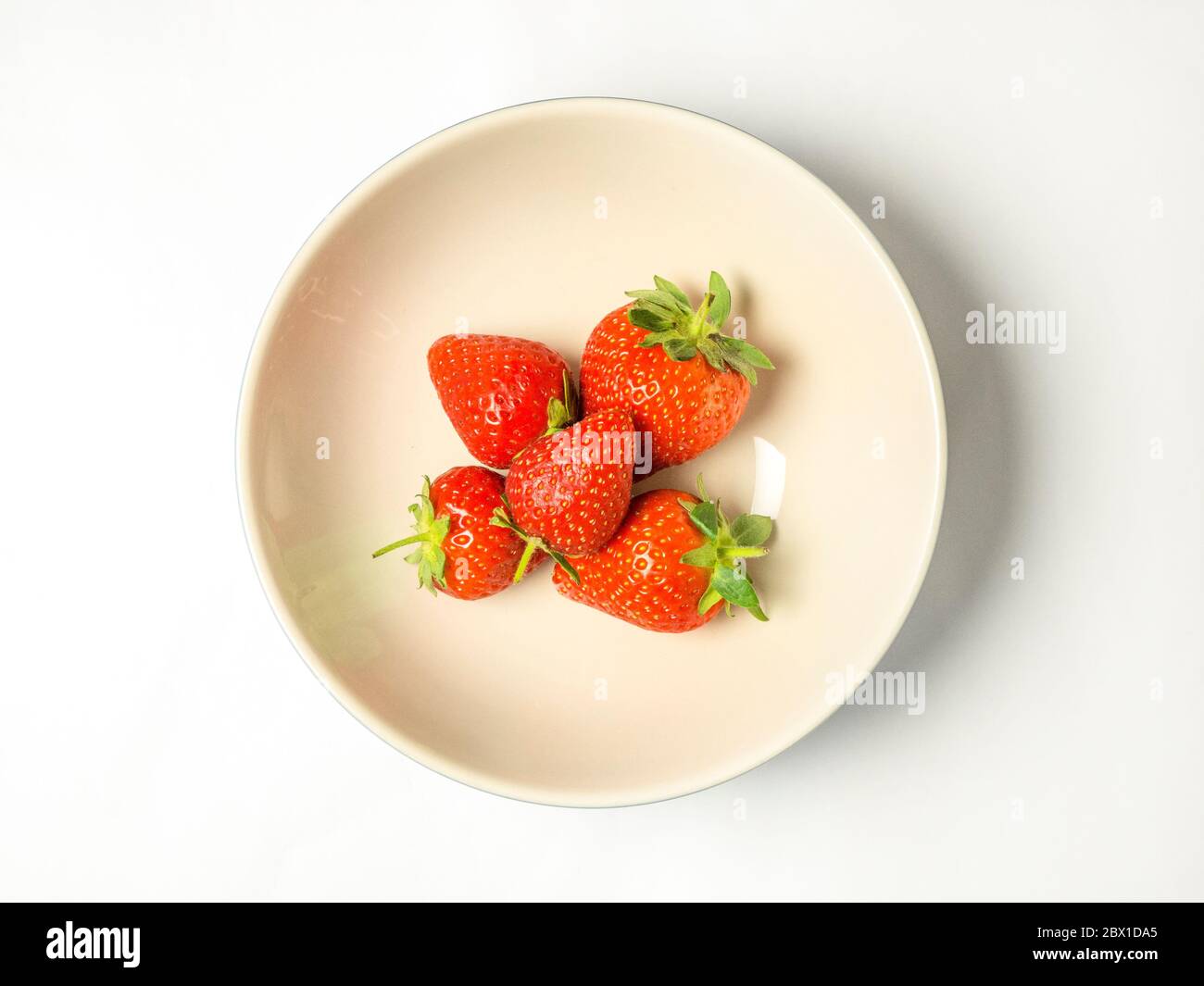 Five fresh strawberries with stalks in a bowl on a white background ...