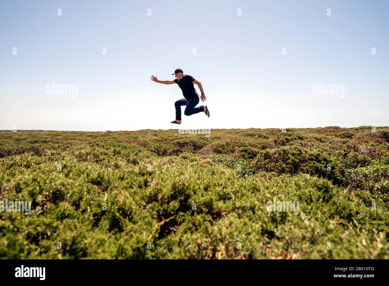 Man happily jumping high above green bushes in Algarve, Portugal Stock ...