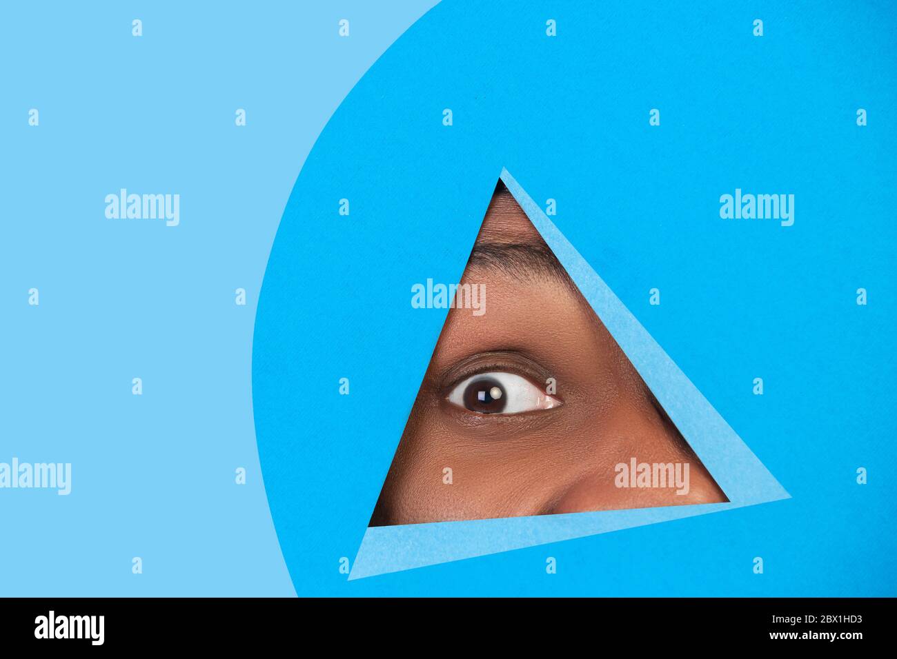 Interested. Eye of african-american man peeks throught triangle in blue ...