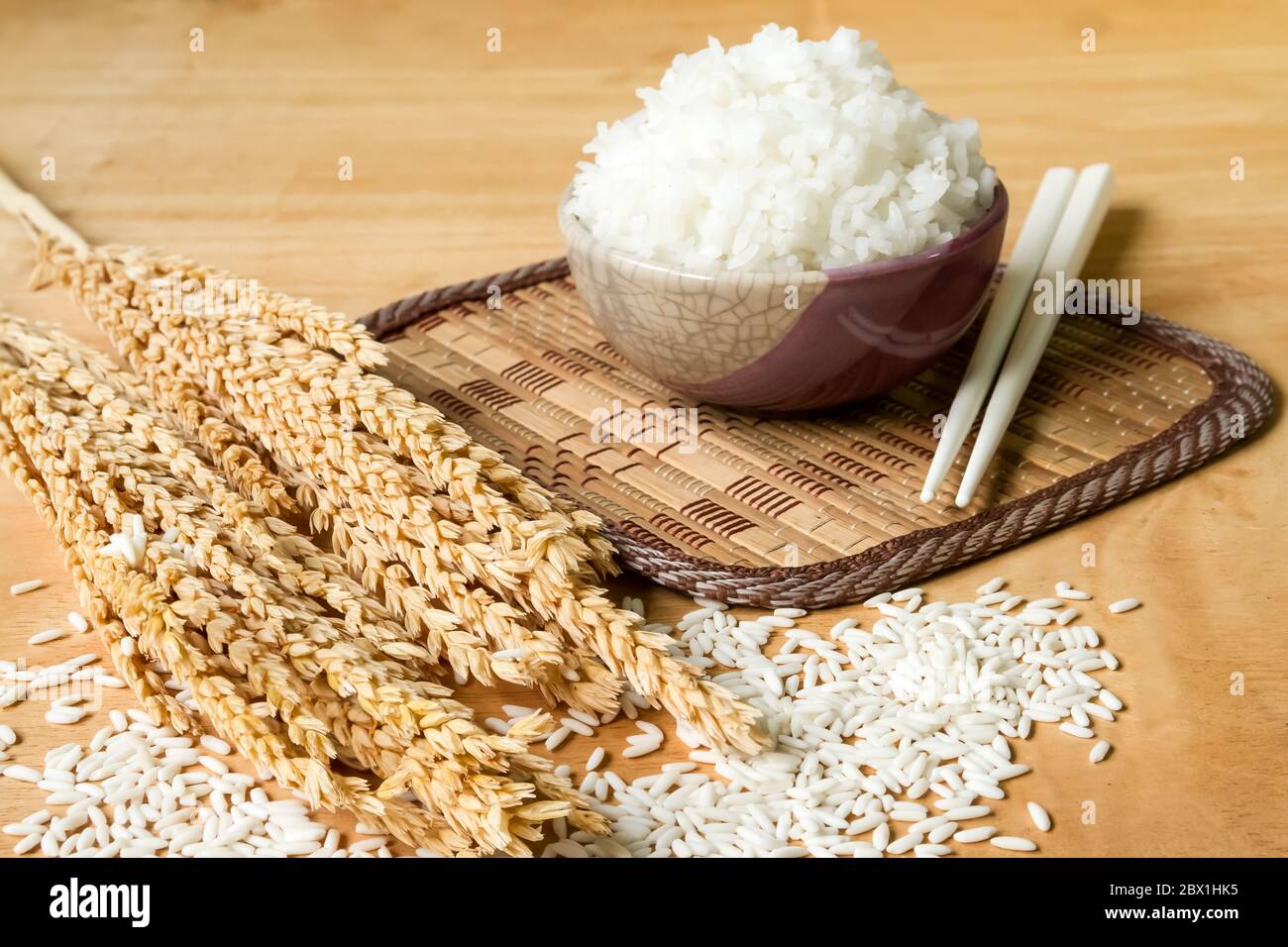 Cooked rice in bowl with raw rice grain and dry rice plant on wooden ...