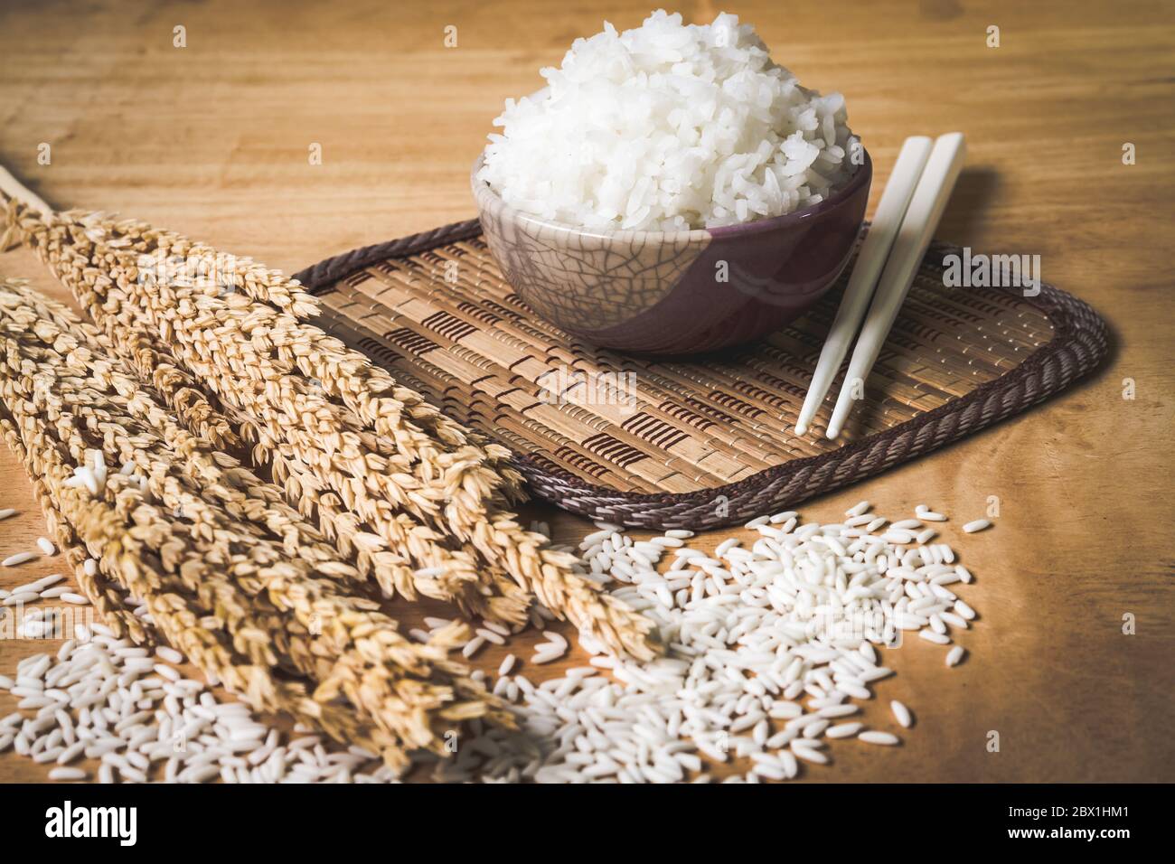 Cooked rice in bowl with raw rice grain and dry rice plant on wooden ...