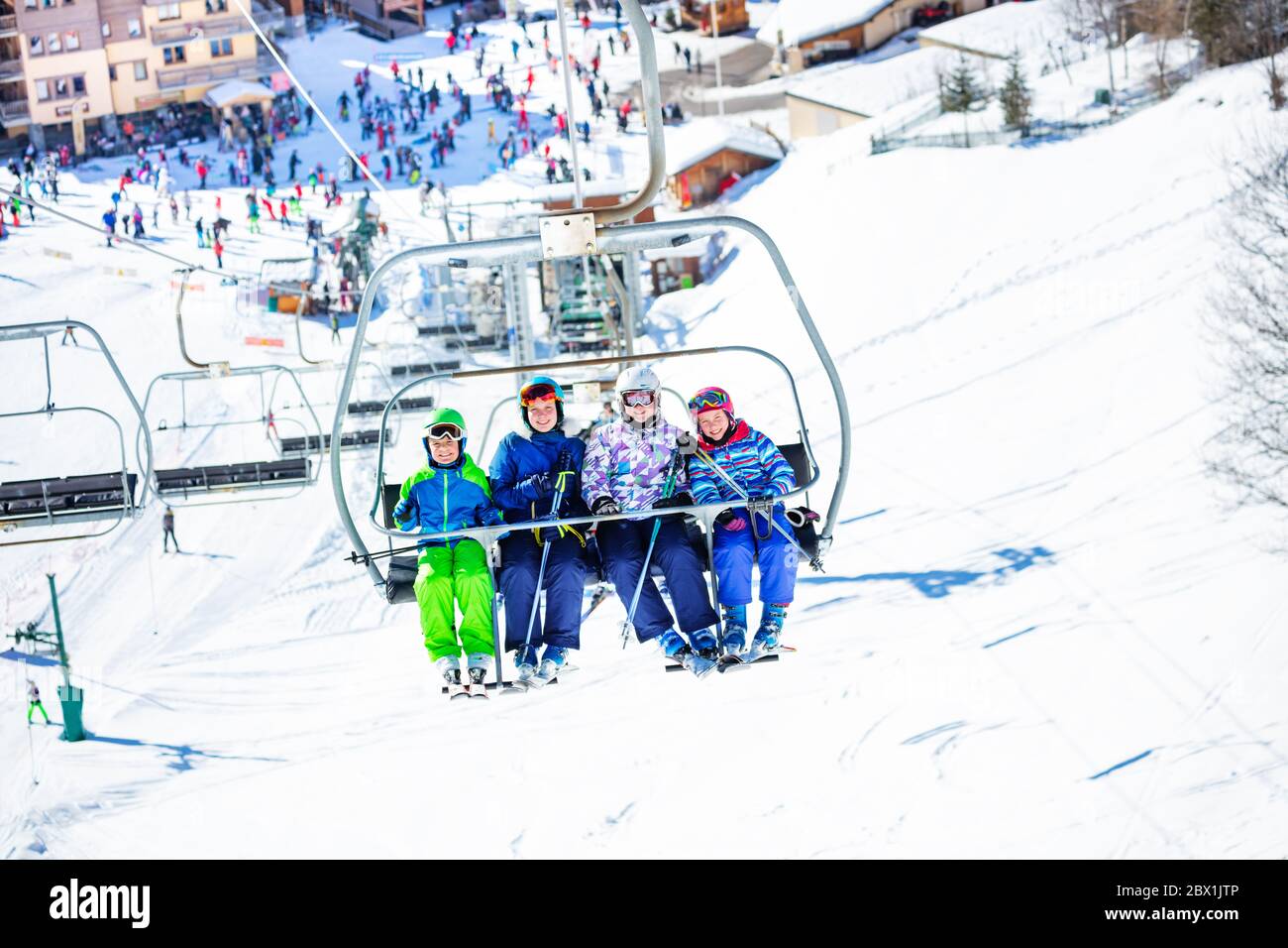 Four friends kids sit together on chairlift lifting on the mountain ...