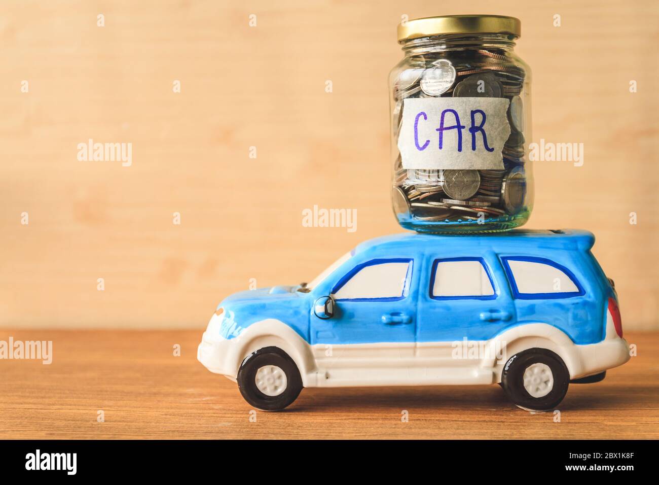 Coins in glass jar with car label and car toy on wooden table ...