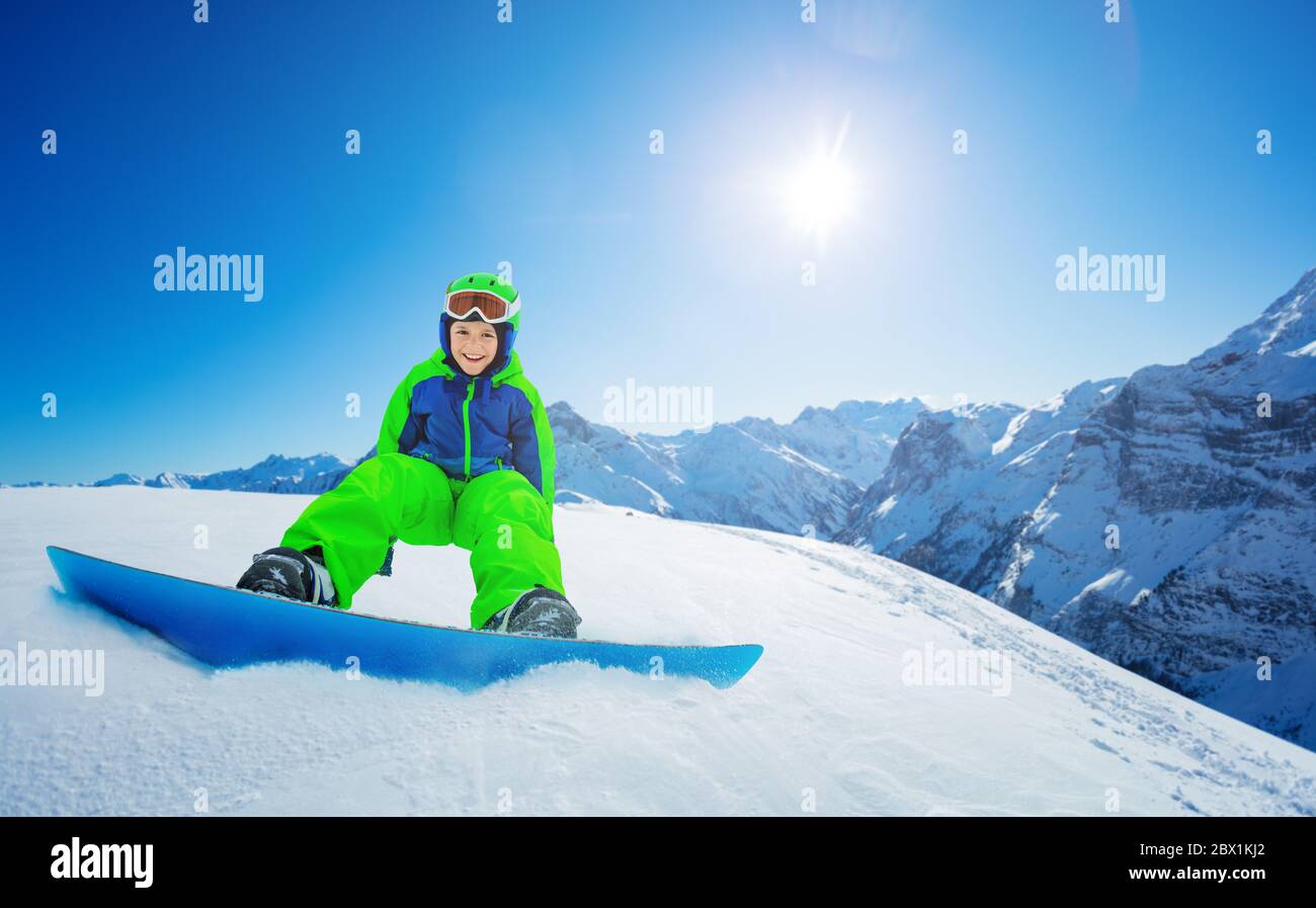 Cute little boy sit on snowboard view over blue sky and mountain range ...
