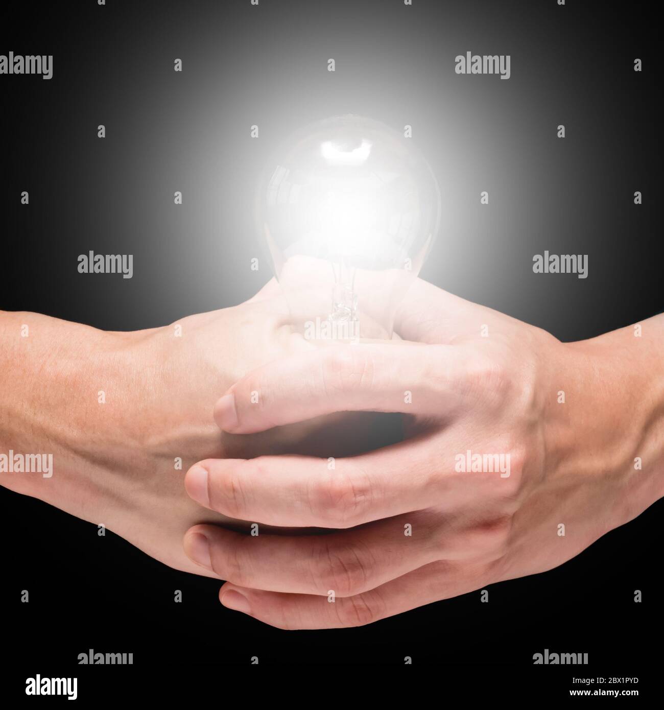 Male hands holding light bulb on a black background Stock Photo - Alamy
