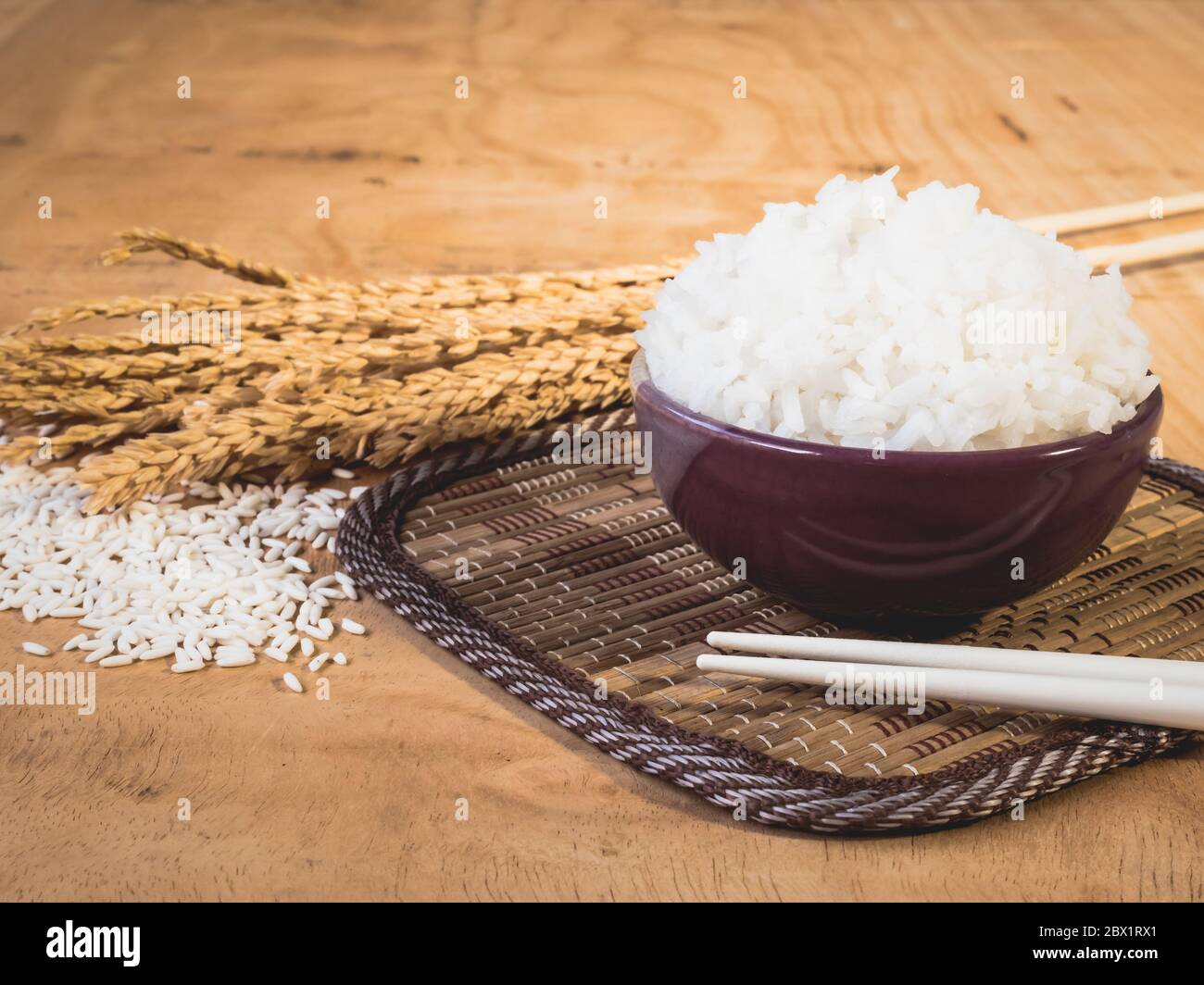 Cooked rice in bowl with raw rice grain and dry rice plant on wooden ...