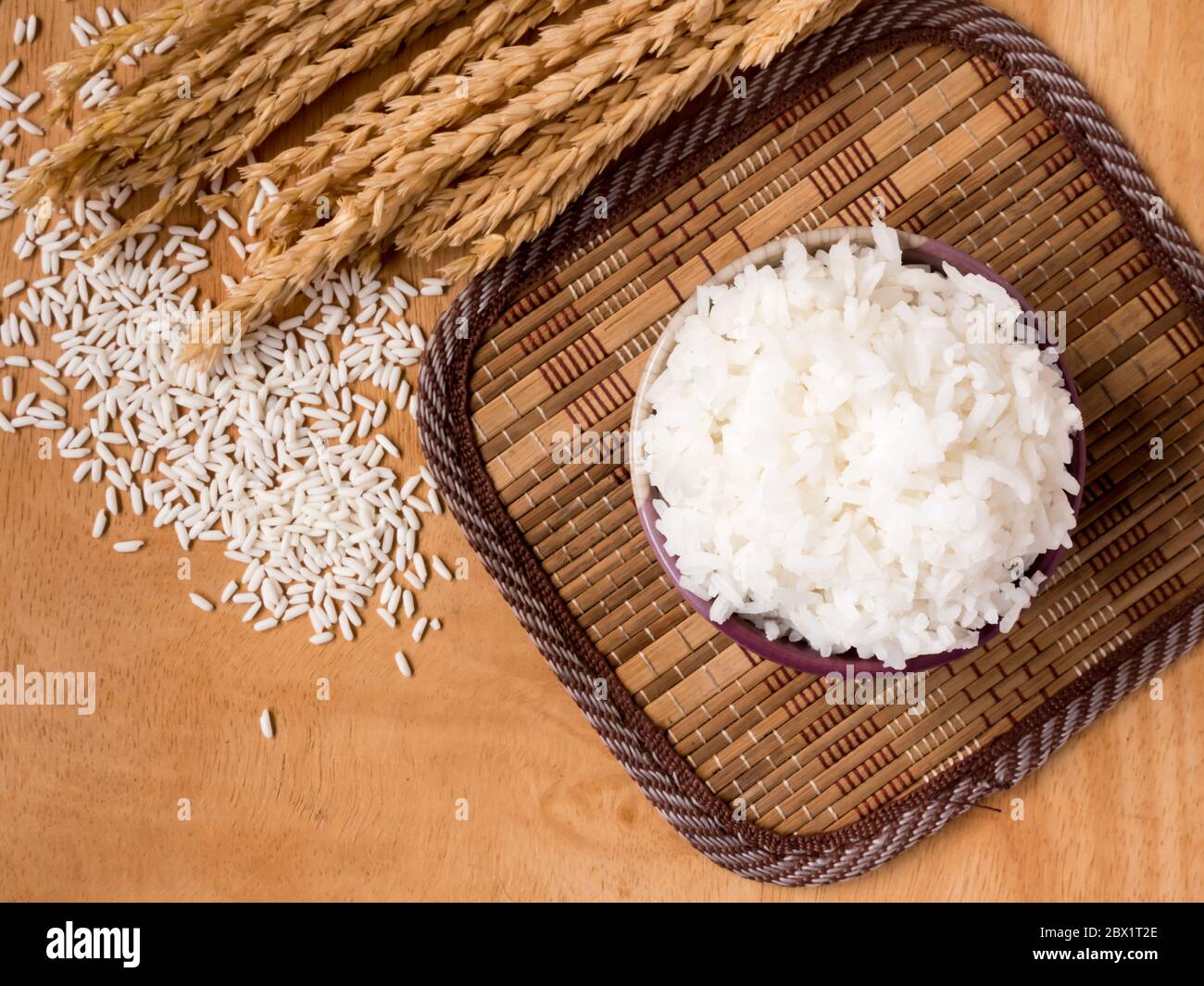 Cooked rice in bowl with raw rice grain and dry rice plant on wooden ...