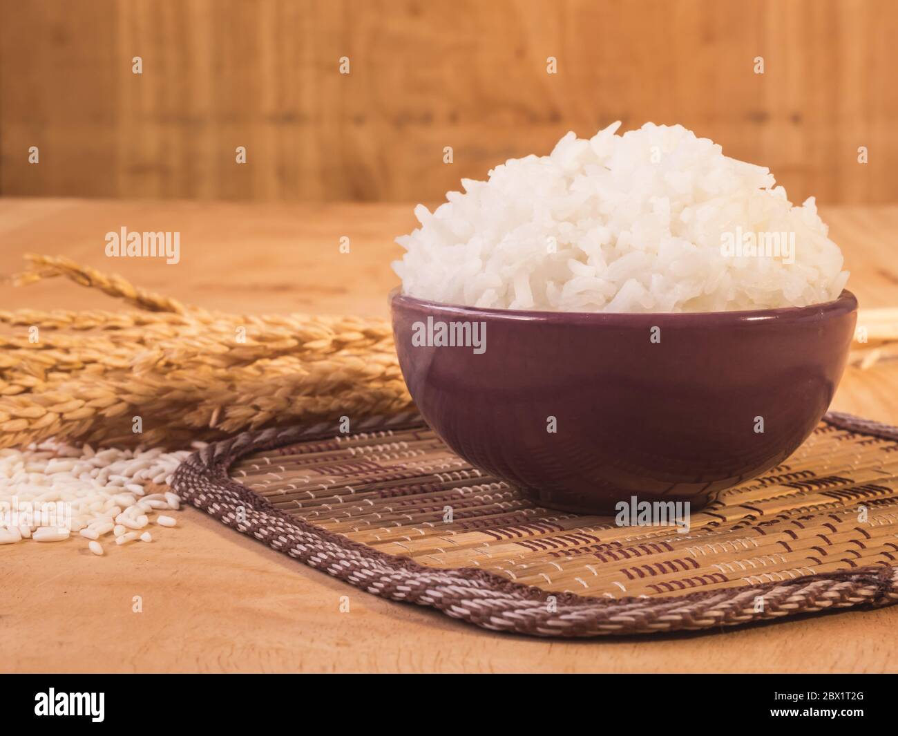 Cooked rice in bowl with raw rice grain and dry rice plant on wooden ...
