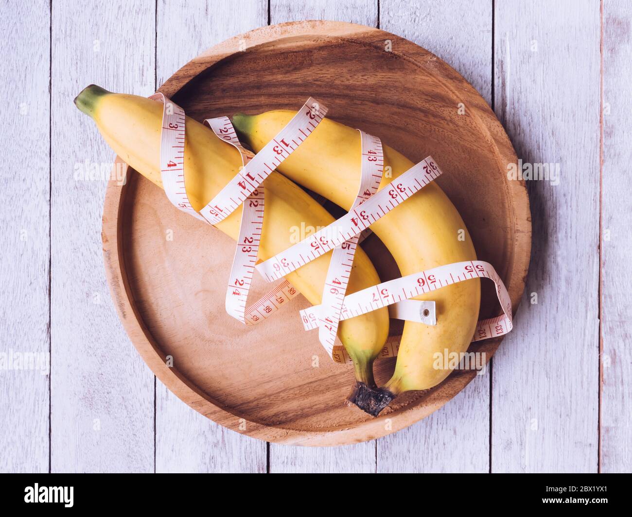 Bananas with measure tape on plate over the wooden table background ...