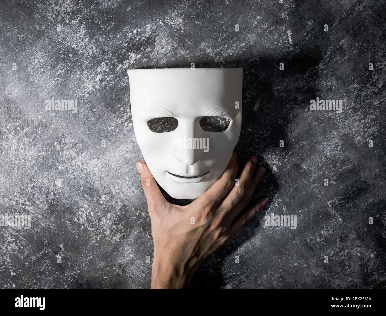 Hand holding white mask on gray grunge background Stock Photo - Alamy