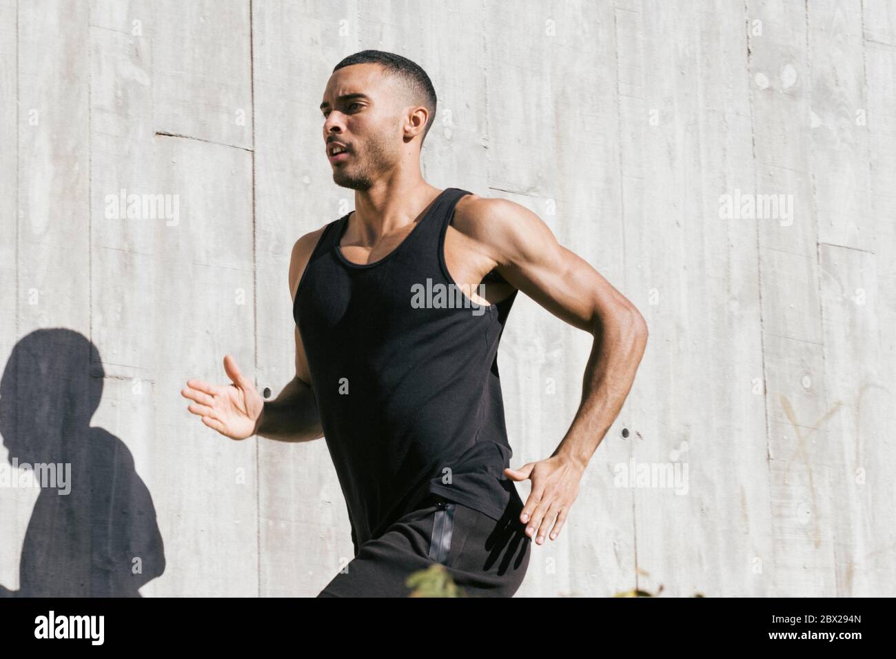 Upper part African American male athlete running against concrete wall ...