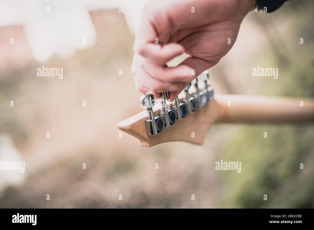 A man tunes a black electric guitar in the open air - twists the ...