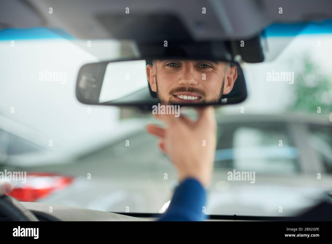 Back view of young handsome man looking and holding small rear view ...