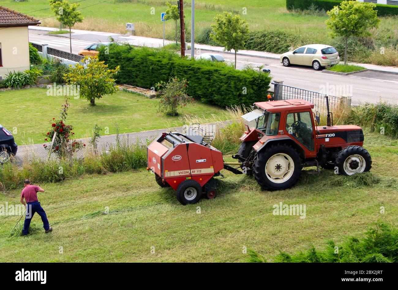 Dairy farmer's tractor towing round hay baler with farmer raking grass ...