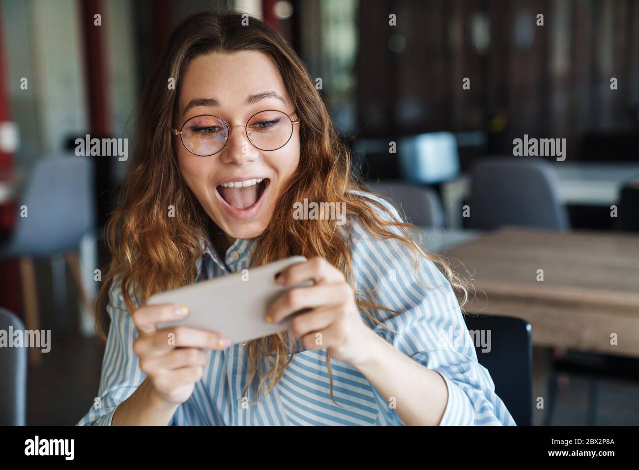 Image of excited charming woman playing video game on cellphone while ...