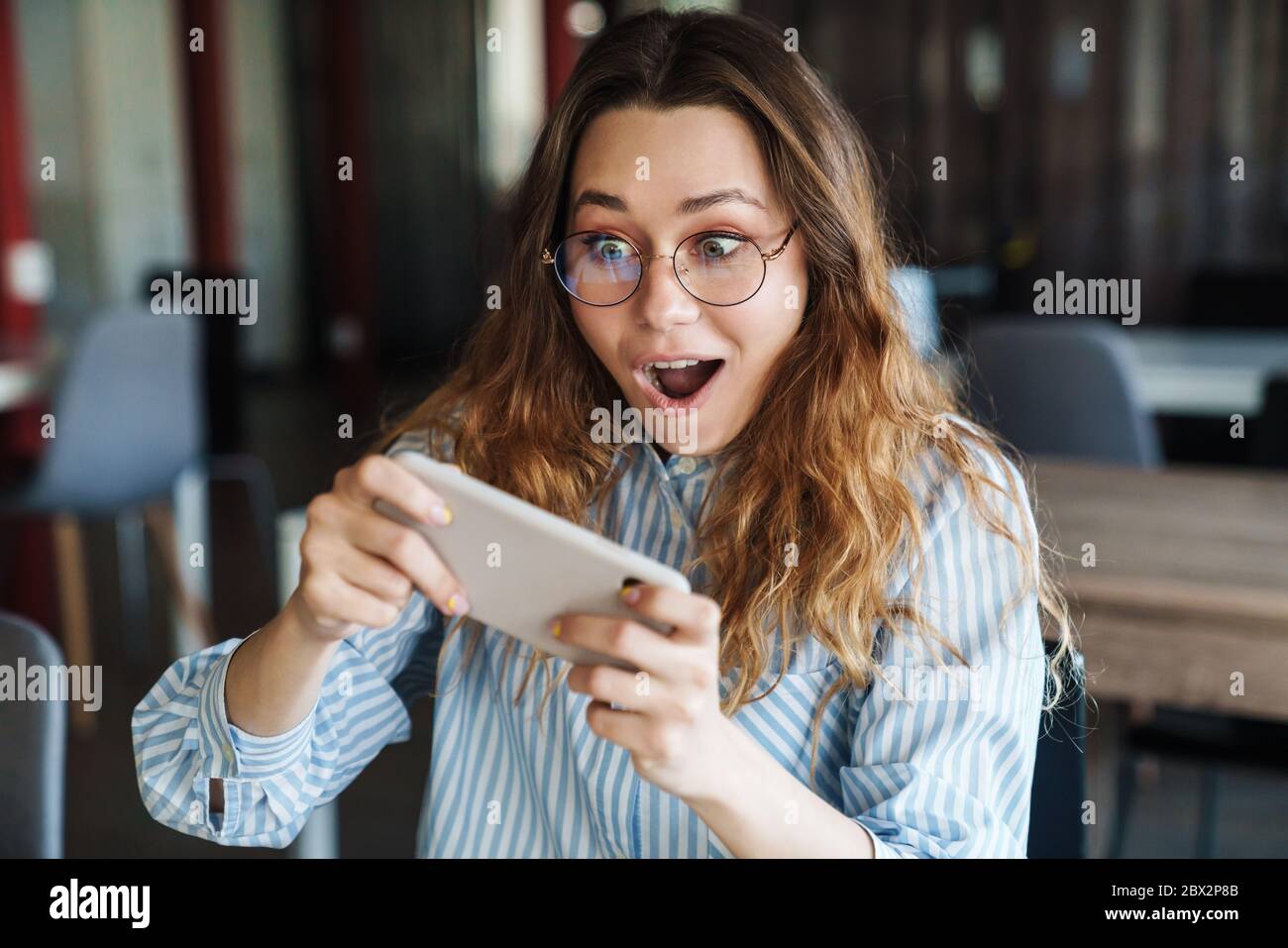 Image of excited charming woman playing video game on cellphone while ...