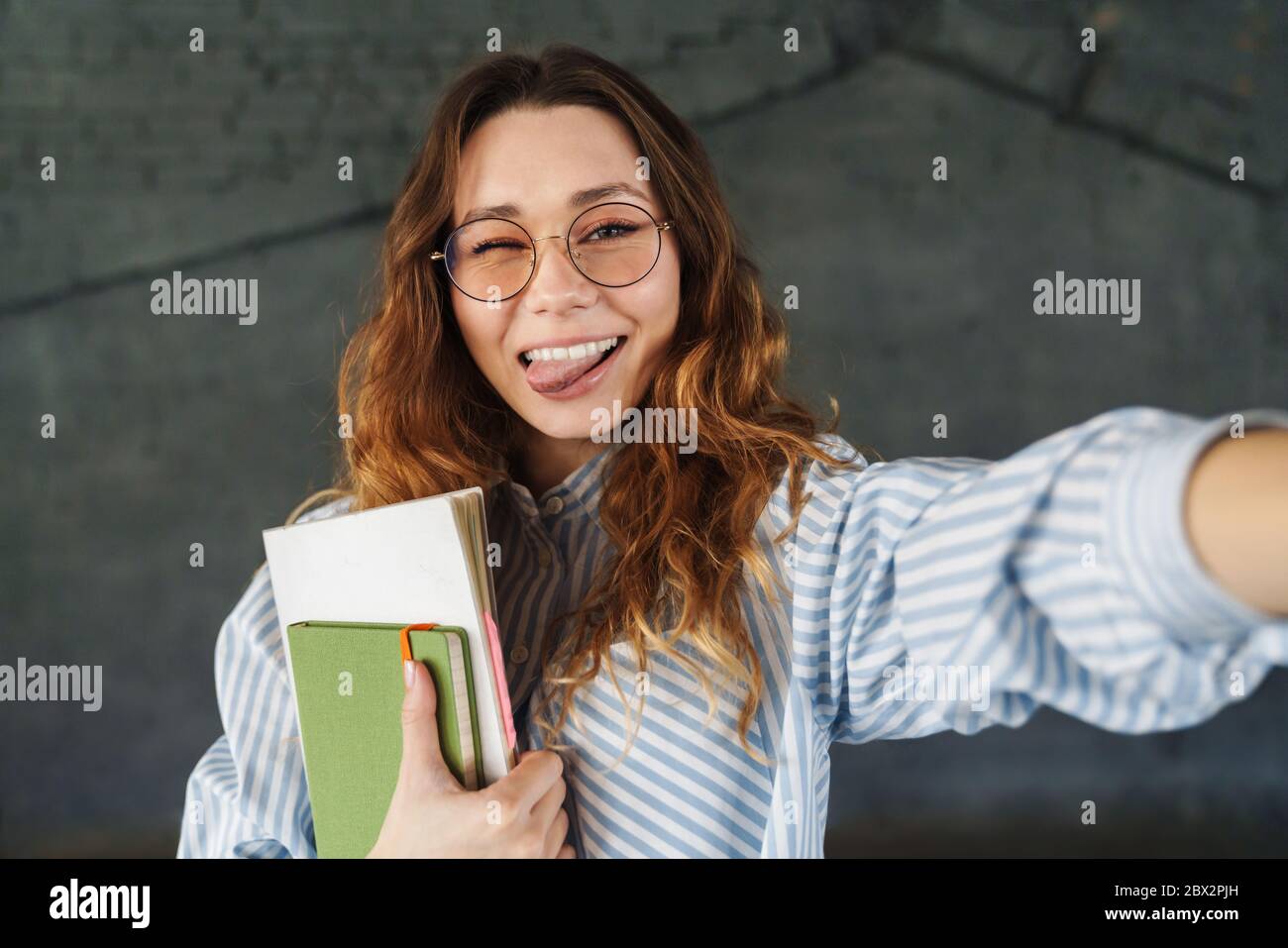 Image of smiling woman winking and holding exercise books while taking ...