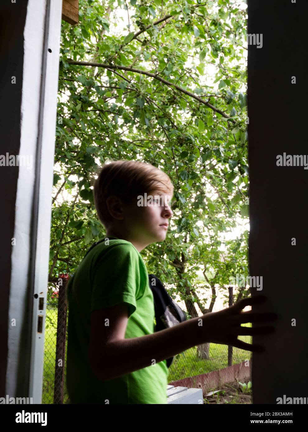 blond-haired Caucasian boy stands in the doorway of a house against a ...