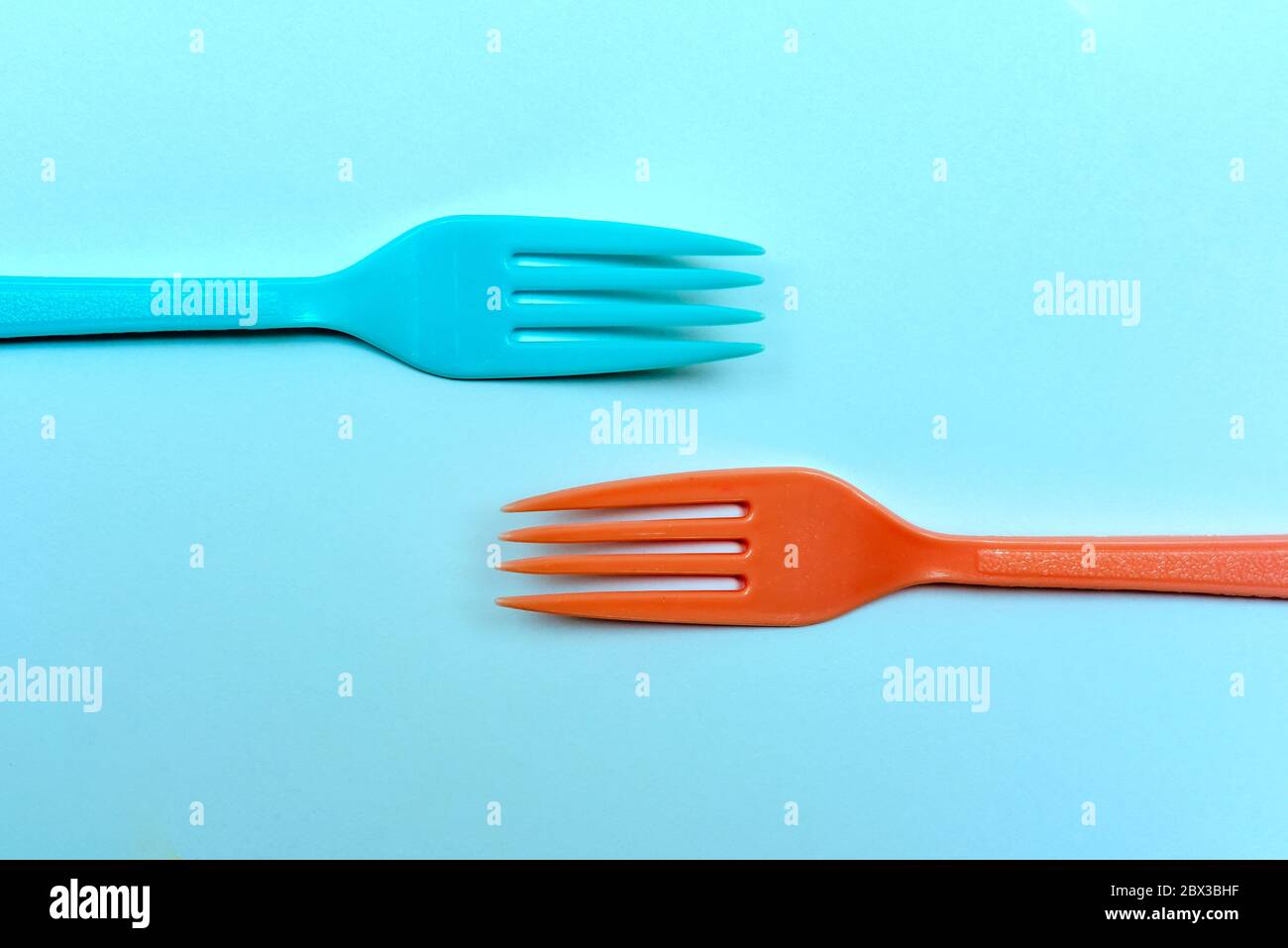 Two brightly colored forks facing towards each other on a ktchen table ...