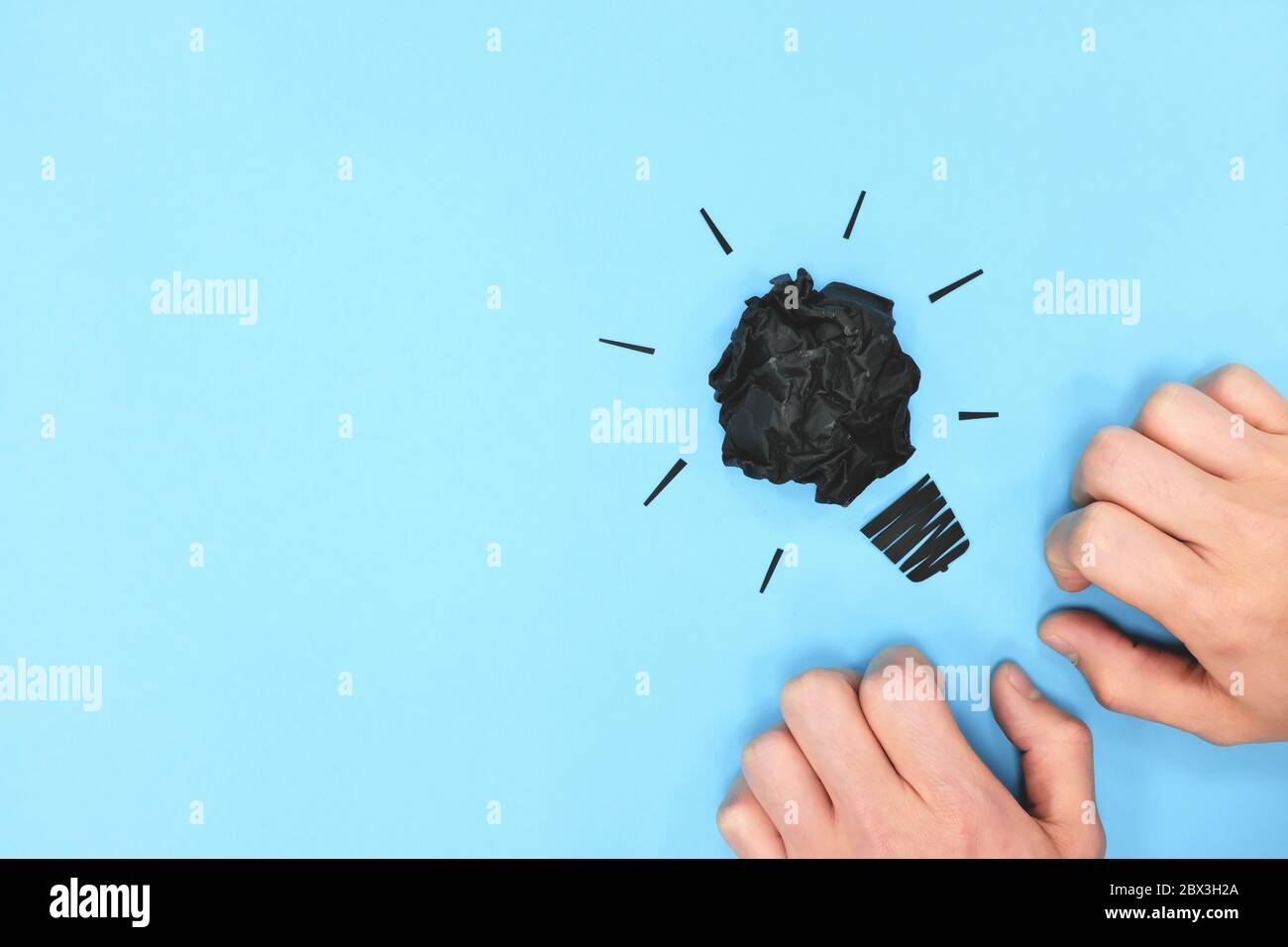 Black light bulb crumpled paper in blue background with hands flat lay ...