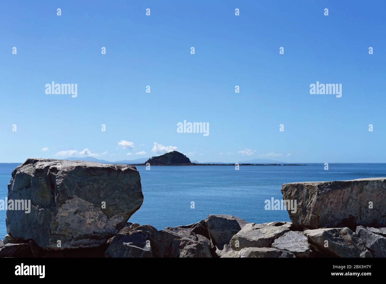Huge rocks on a harbour wall frame a small island on the horizon ...