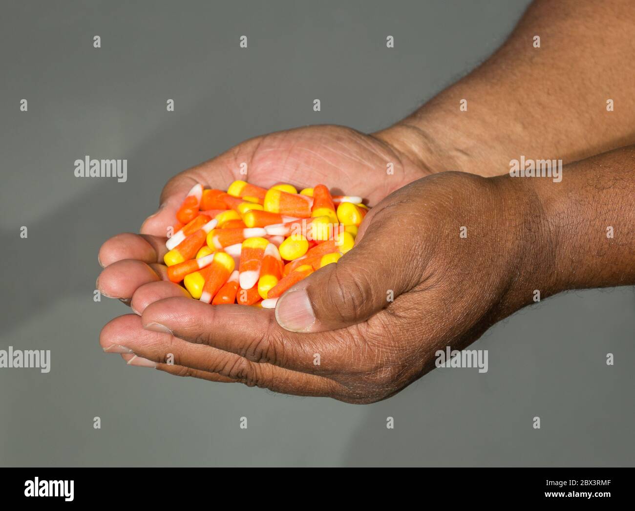 a black man's cupped hands filled with orange, yellow and white candy ...