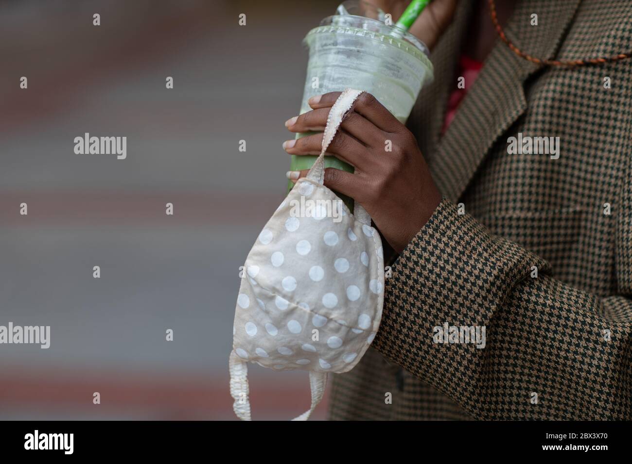 Hand holding a face mask and a beverage in a cup. Face masks are ...