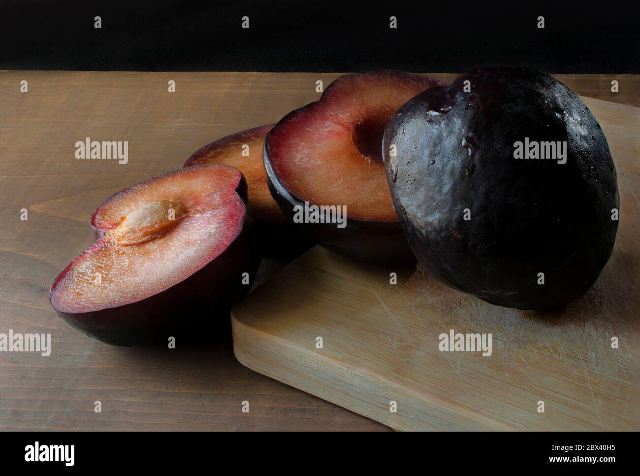 Plums cut in half showing the seed. on a cutting board made of wood and ...