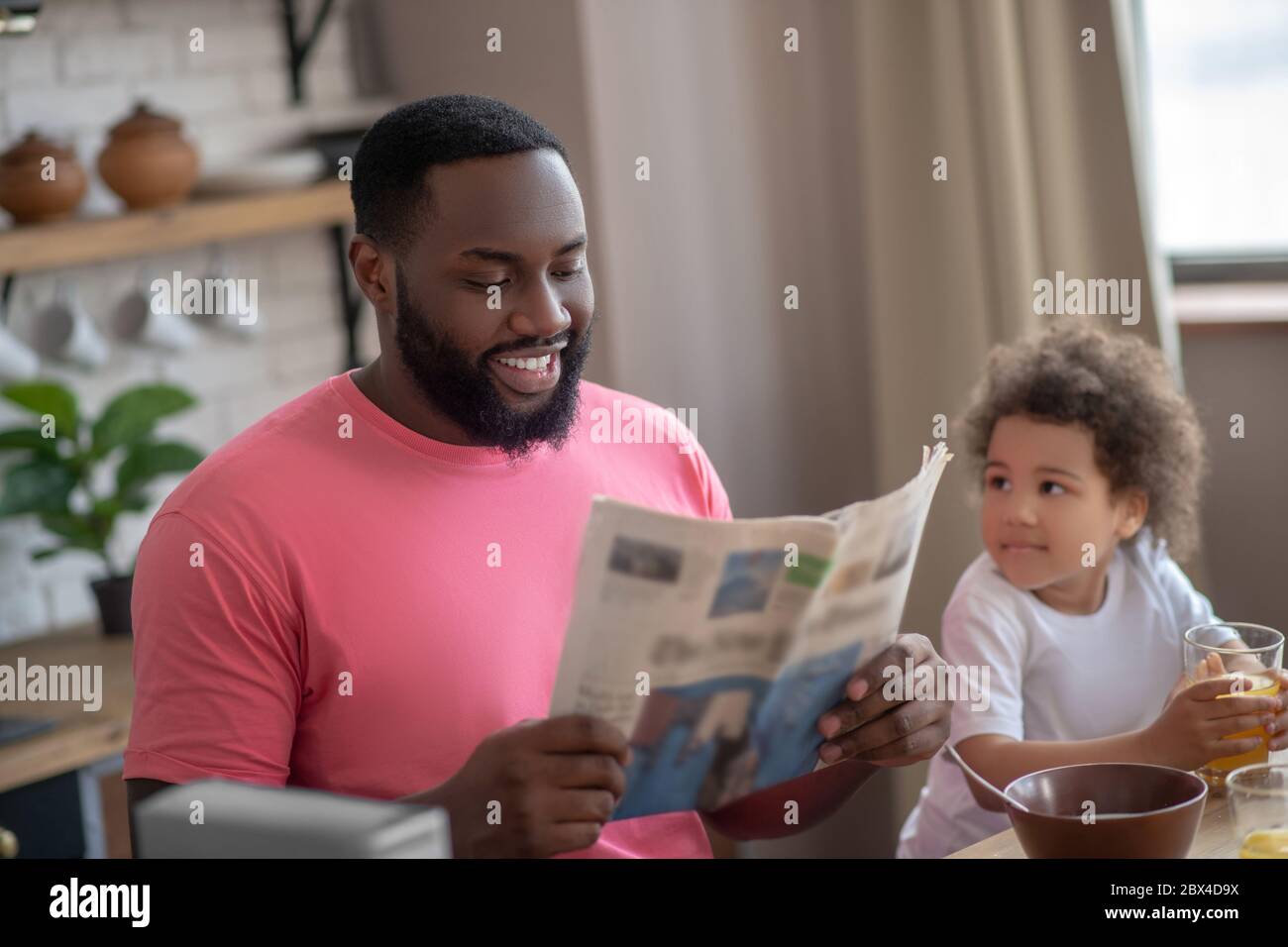 Dark-haired african american father reading a newspaper while having ...