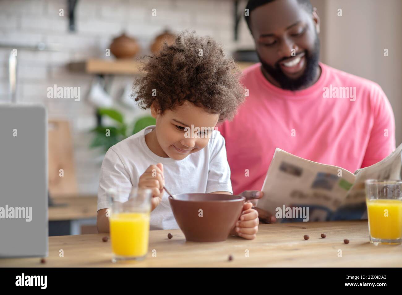 Dark-haired african american father reading a newspaper while his kid ...