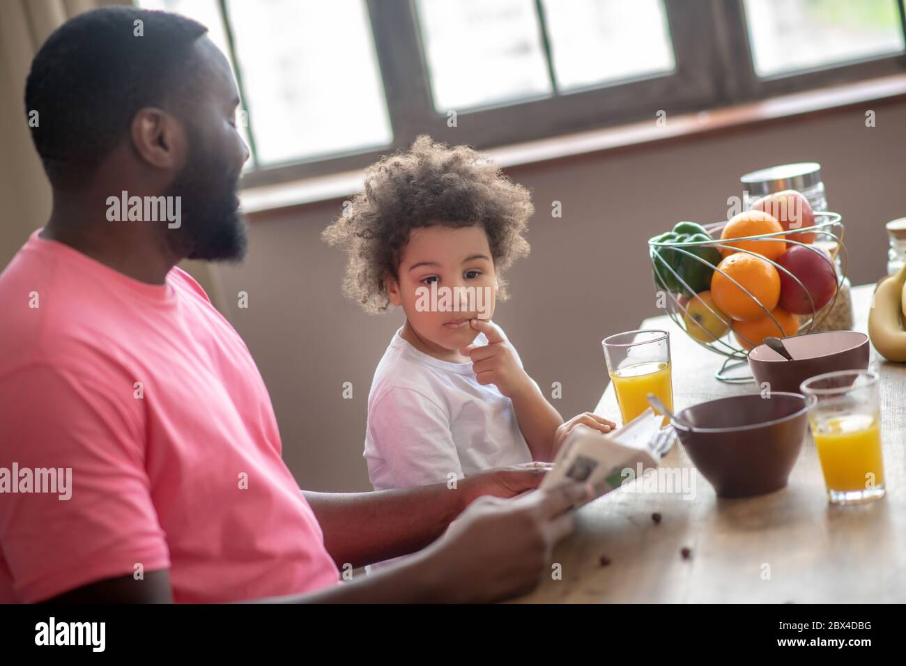 Dark-haired african american father reading a newspaper while having ...