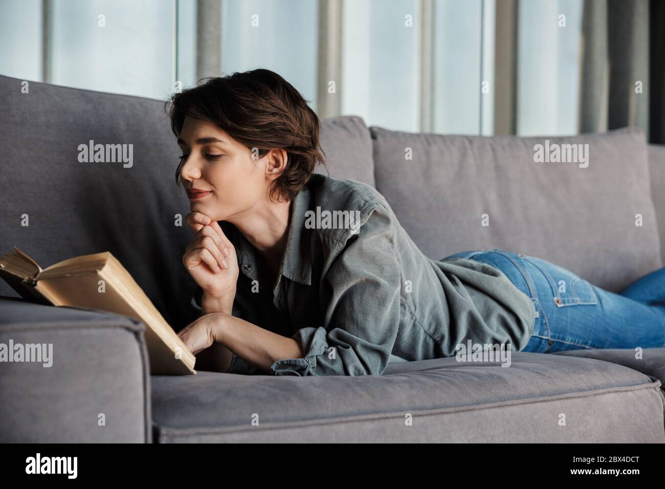 Image of brunette cute pleased woman reading book and smiling while ...