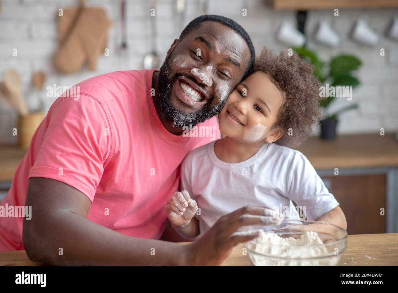 Dark-skinned father looking funny with face stained with flour, his ...