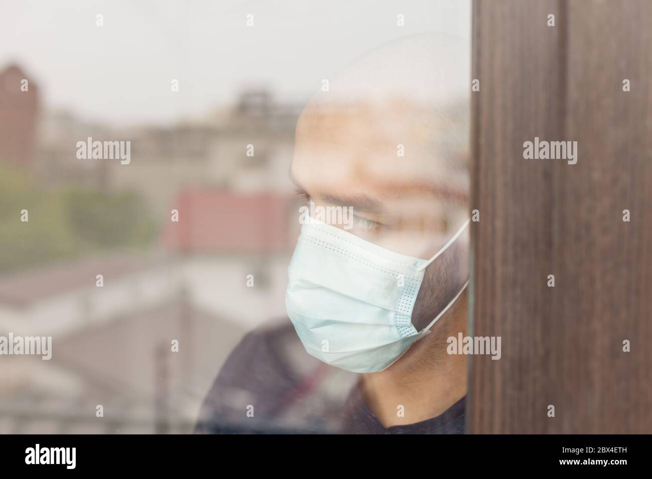 Lonely man looking outside through window glass during self isolation ...