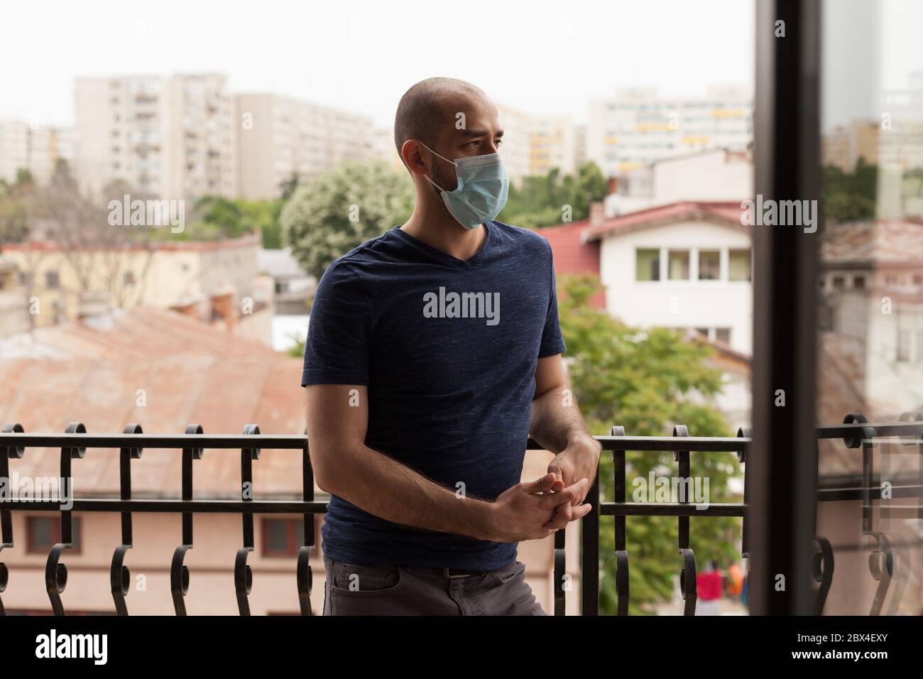 Guy with face mask relaxing on apartment balcony during self isolation ...