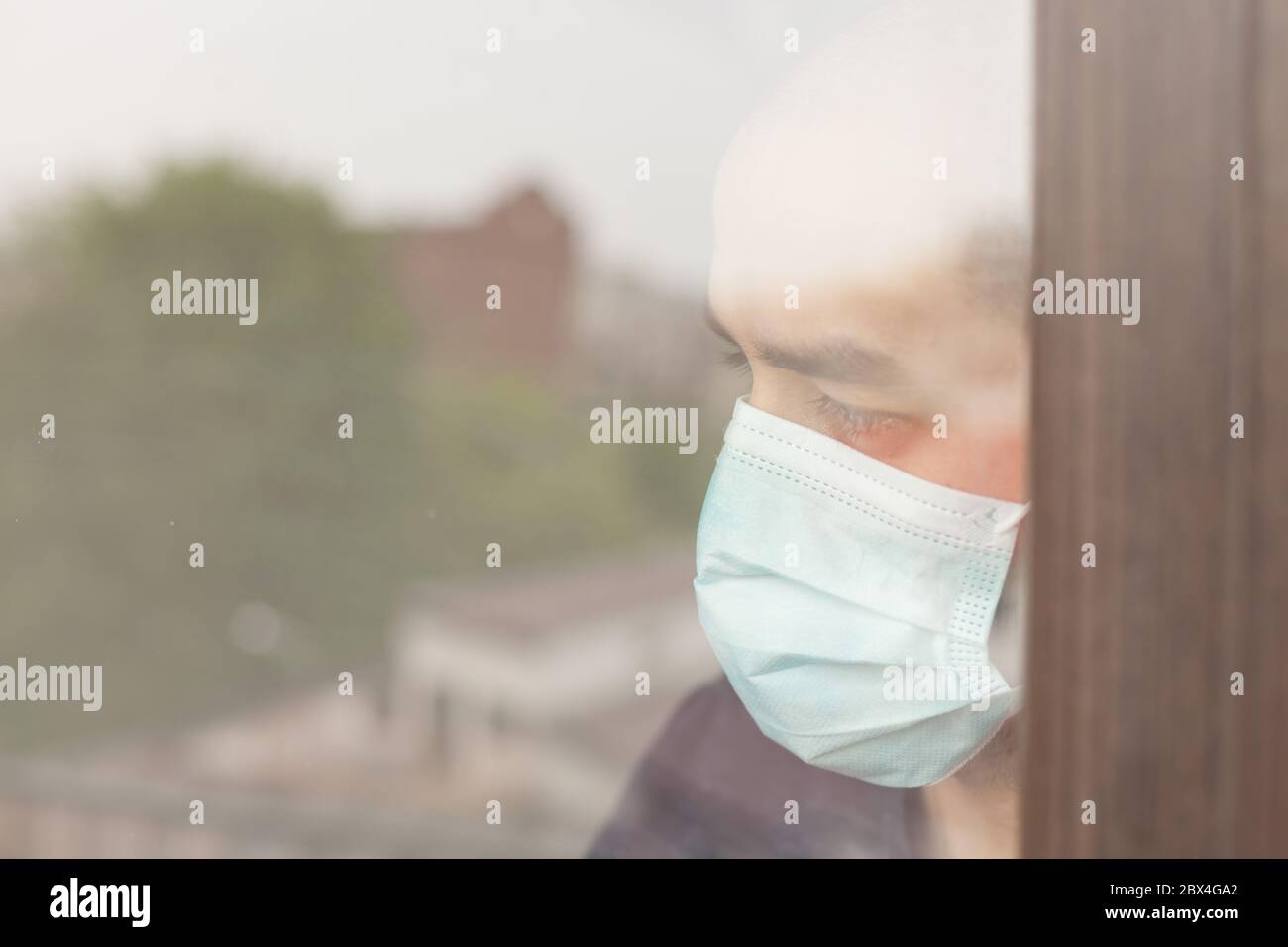 Depressed man looking through window during self isolation Stock Photo ...