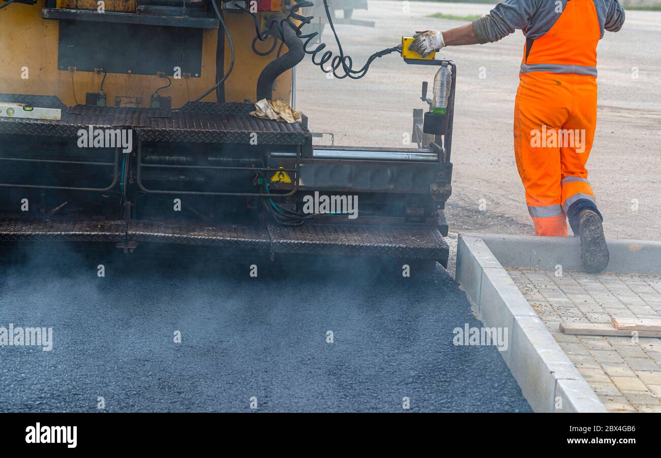 Workers regulate tracked paver laying asphalt heated to temperatures ...