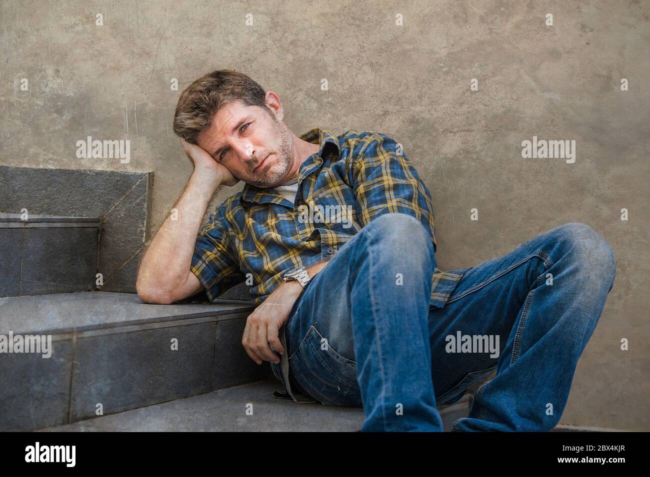 young sad and desperate man sitting outdoors at street stairs suffering ...