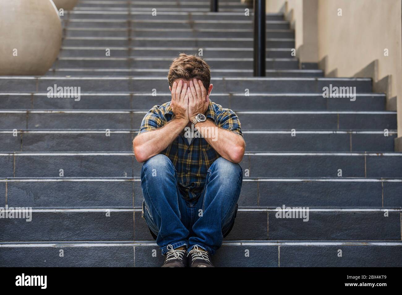young sad and desperate man sitting outdoors at street stairs suffering ...
