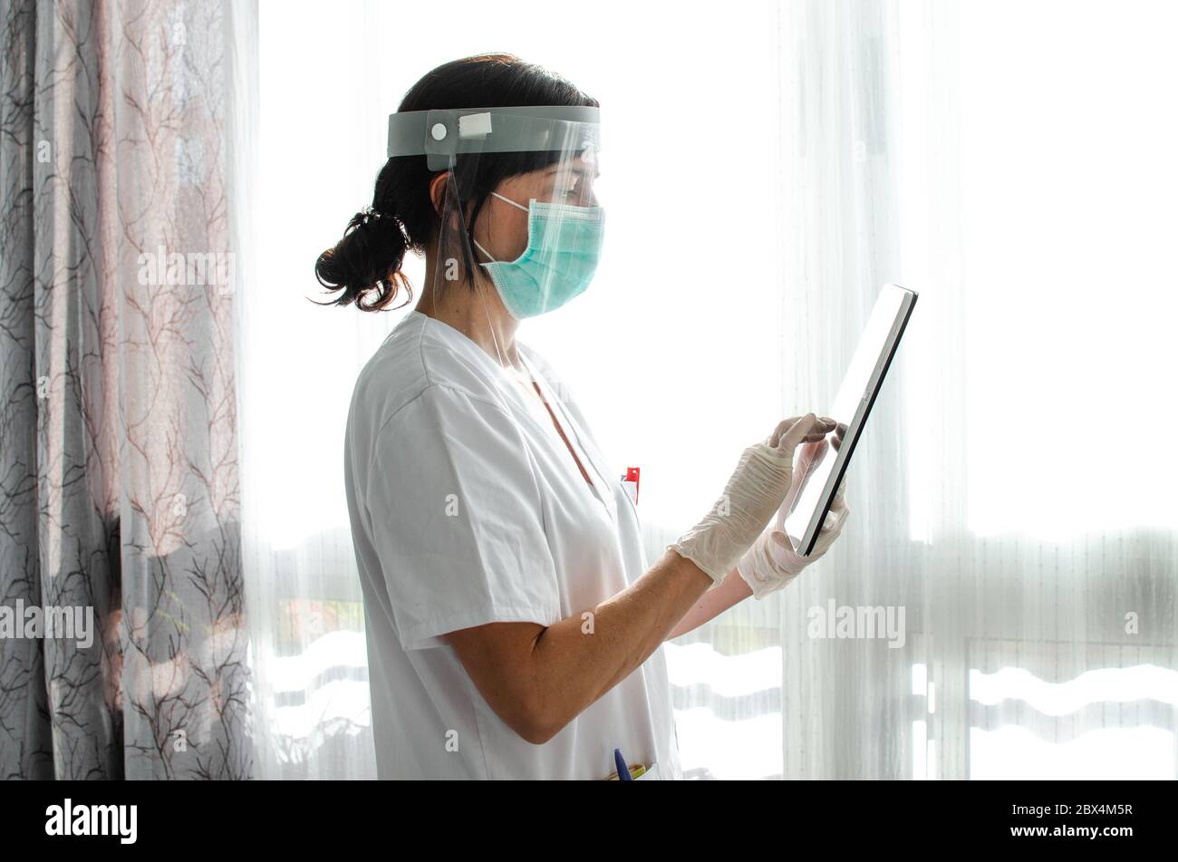 Nurse with a face shield using a tablet. Side view Stock Photo - Alamy