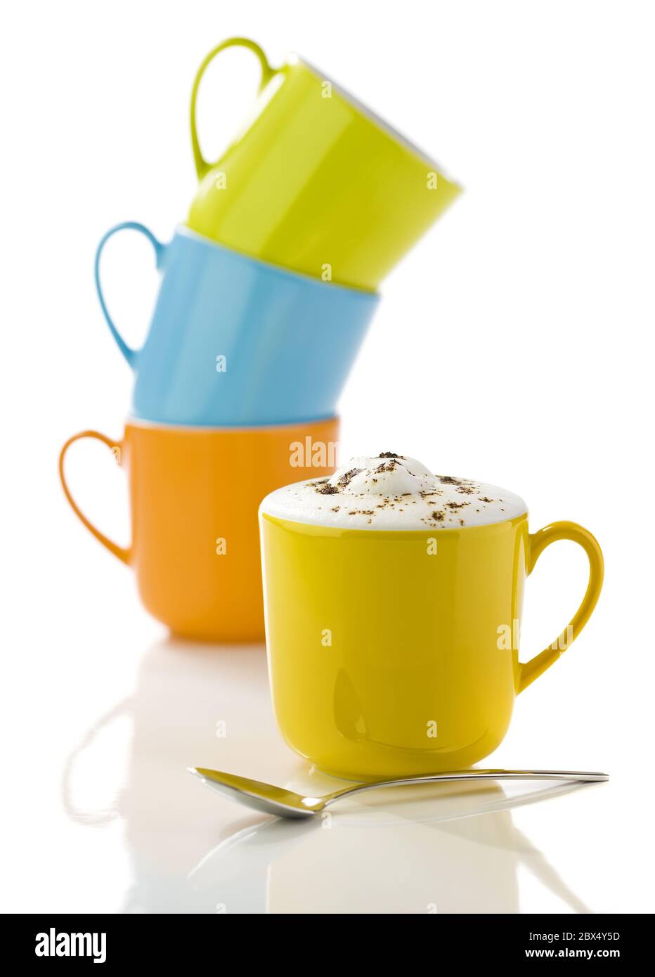 yellow mug filled with cappuccino, spoon in front, green, orange and ...