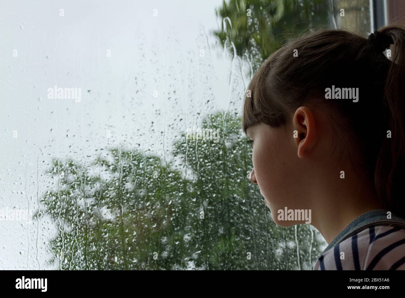 Girl looking through rain covered window Stock Photo - Alamy