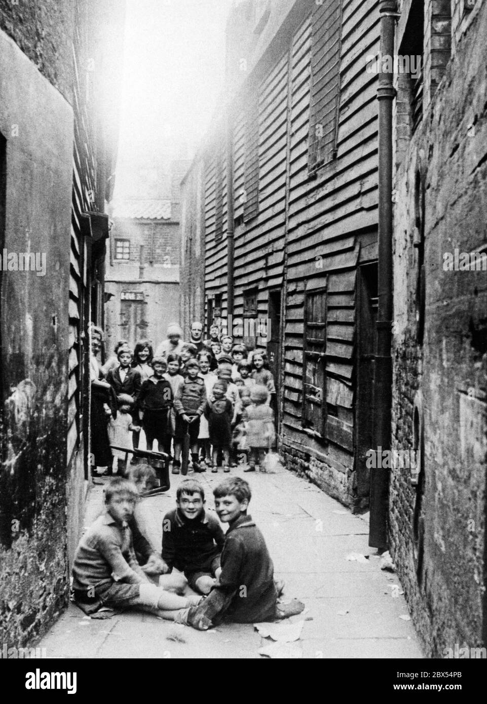 Three children sit in a narrow alleyway in a tenement building in ...