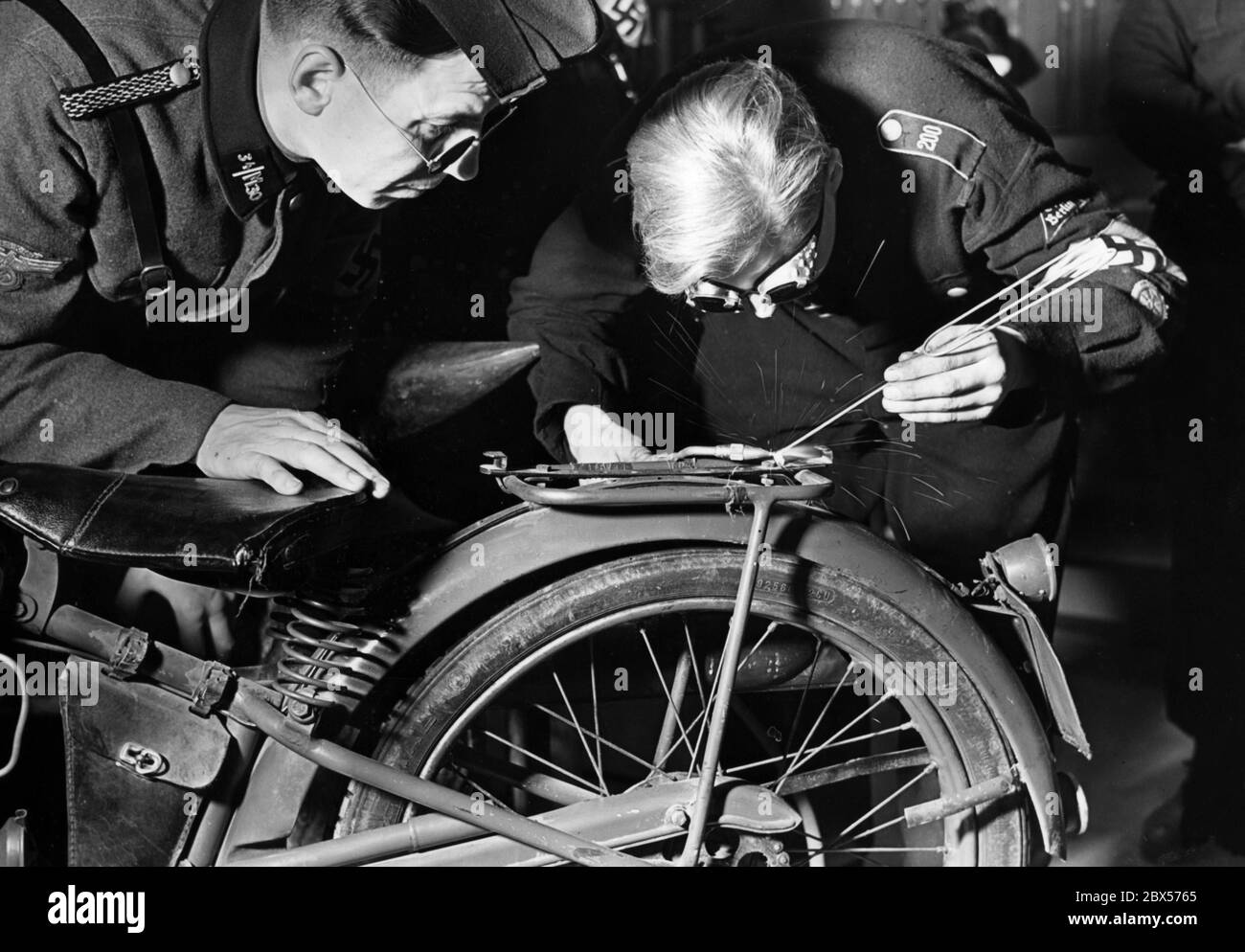 A member of the Motor Hitler Youth welds on a motorcycle while an NSKK ...