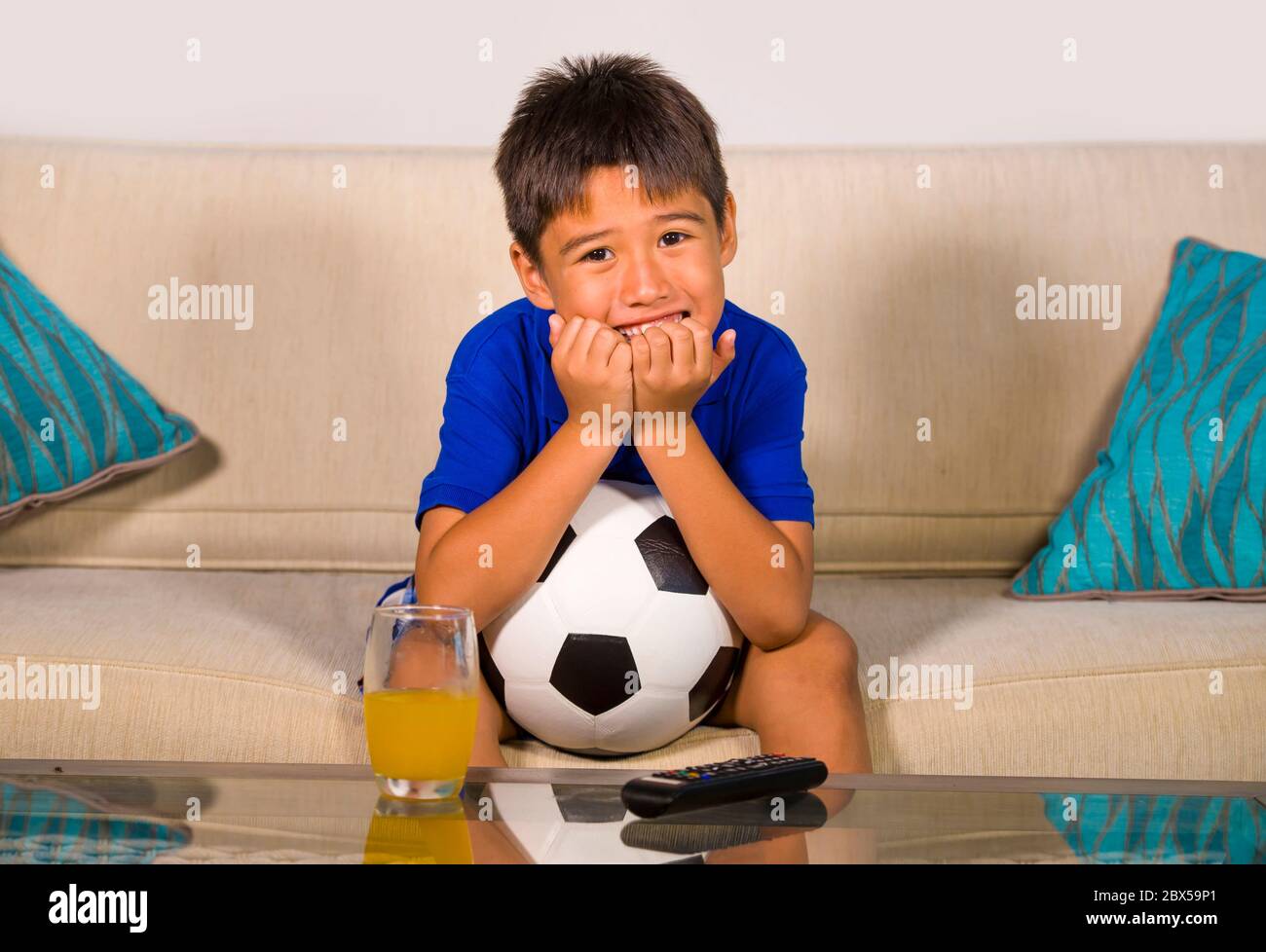 lifestyle portrait at home of young boy holding soccer ball watching ...