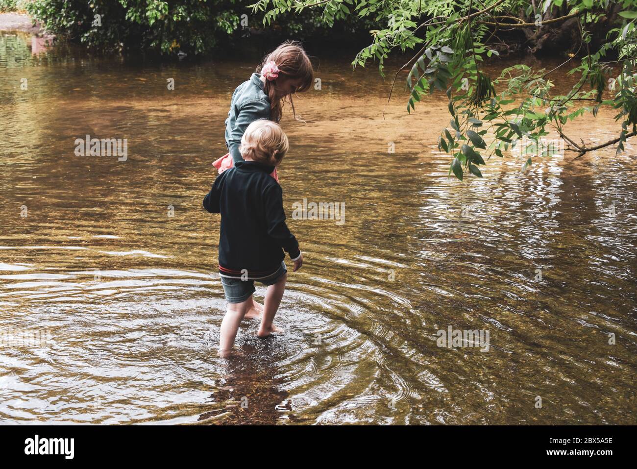 Children playing outside in a shallow stream paddling in the water ...